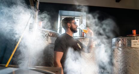 Man tasting beer with large brews behind him during the Beer Masterclass at the Walled City Brewery in Derry~Londonderry