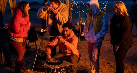 Group at night-time around a camp fire enjoying the Mussenden Unwind experience