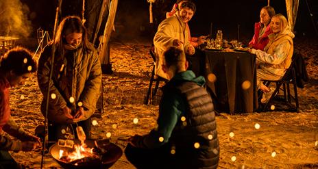 Group on the beach at night-time enjoying refreshments as part of the Mussenden Unwind experience