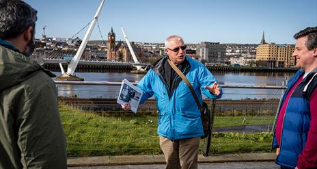 Group listening to guide David from Derrie Danders with the Peace Bridge in the background