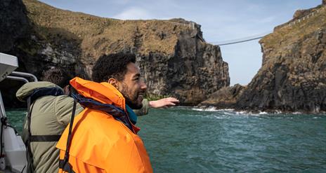 Group on a boat with Carrick-a-Rede Rope Bridge in the background as part of a scuba diving experience with Aquaholics 