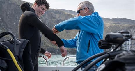 Man on a boat being assisted with his outfit by the guide as part of a scuba diving experience with Aquaholics 