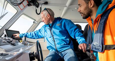 The guide/skipper of the boat showing a guest the instruments on the boat as part the Giant Shipwrecks of the North Coast experience with Carrick-A-Re