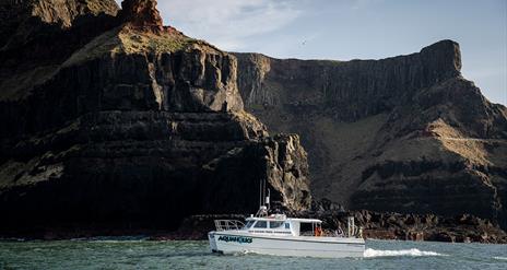 The Aquaholics boat used in the Giant Shipwrecks of the North Coast experience with cliffs in the background
