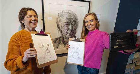 A couple of women take a selfie showing their attempts at sketching an image of Seamus Heaney